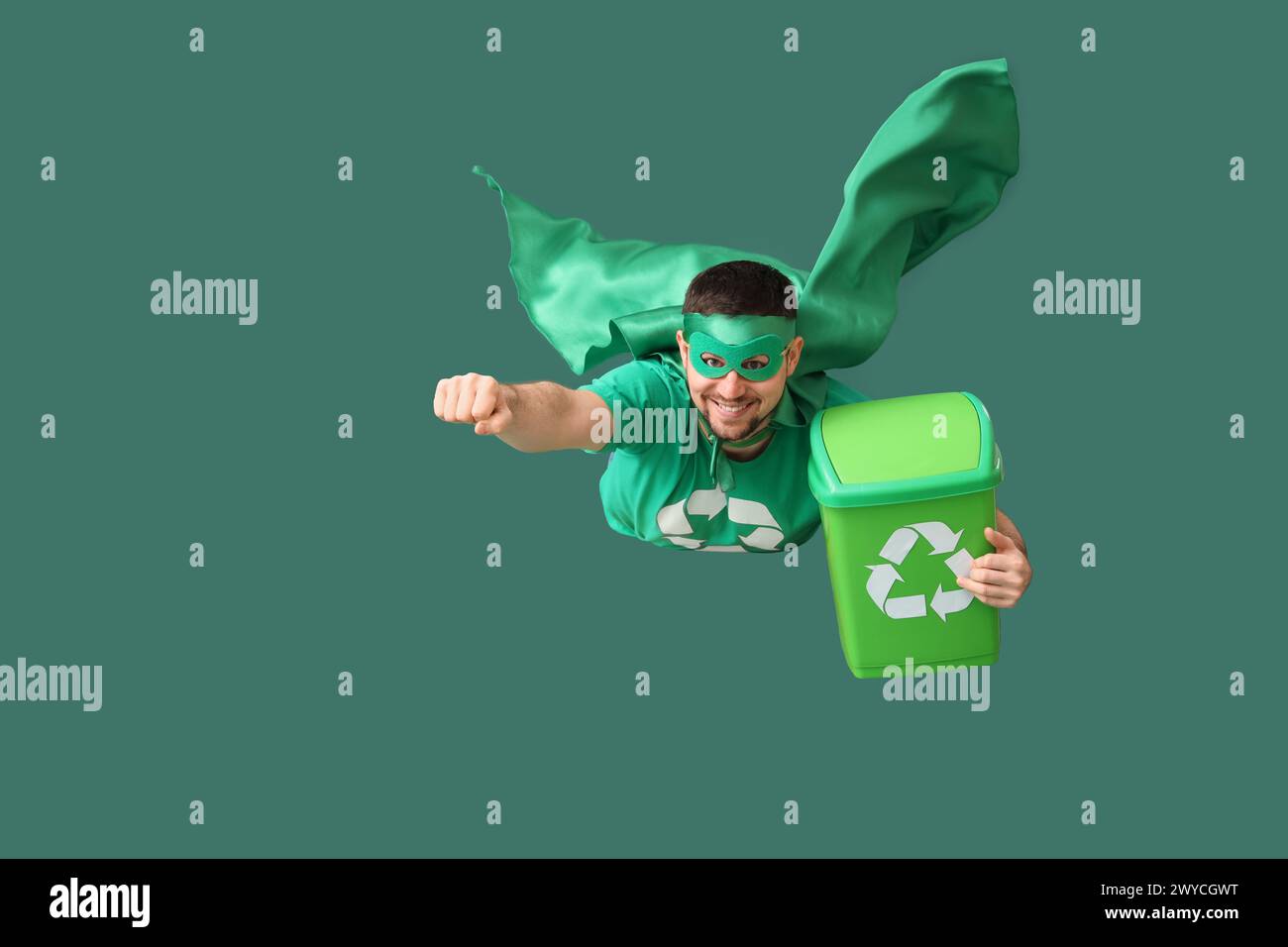 Young man dressed as eco superhero flying with garbage bin on green ...