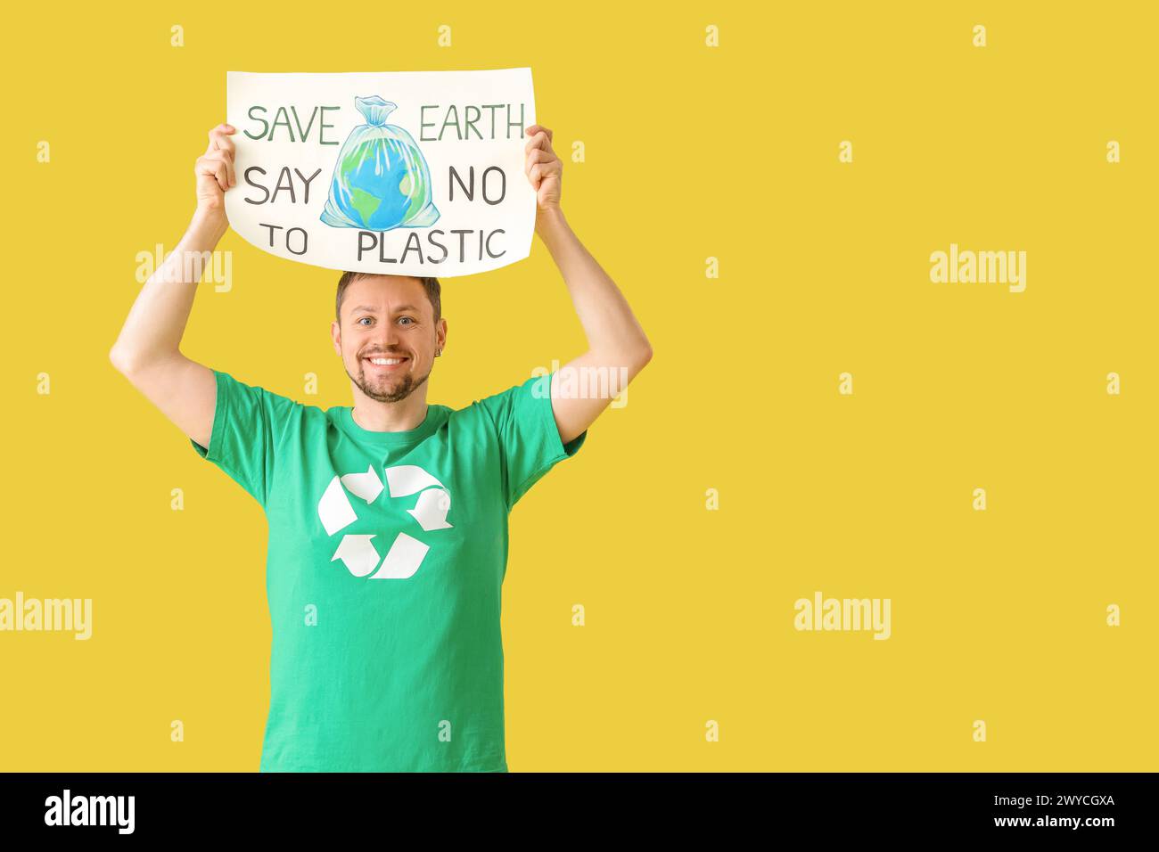 Happy young man in t-shirt with recycling logo holding poster with text ...