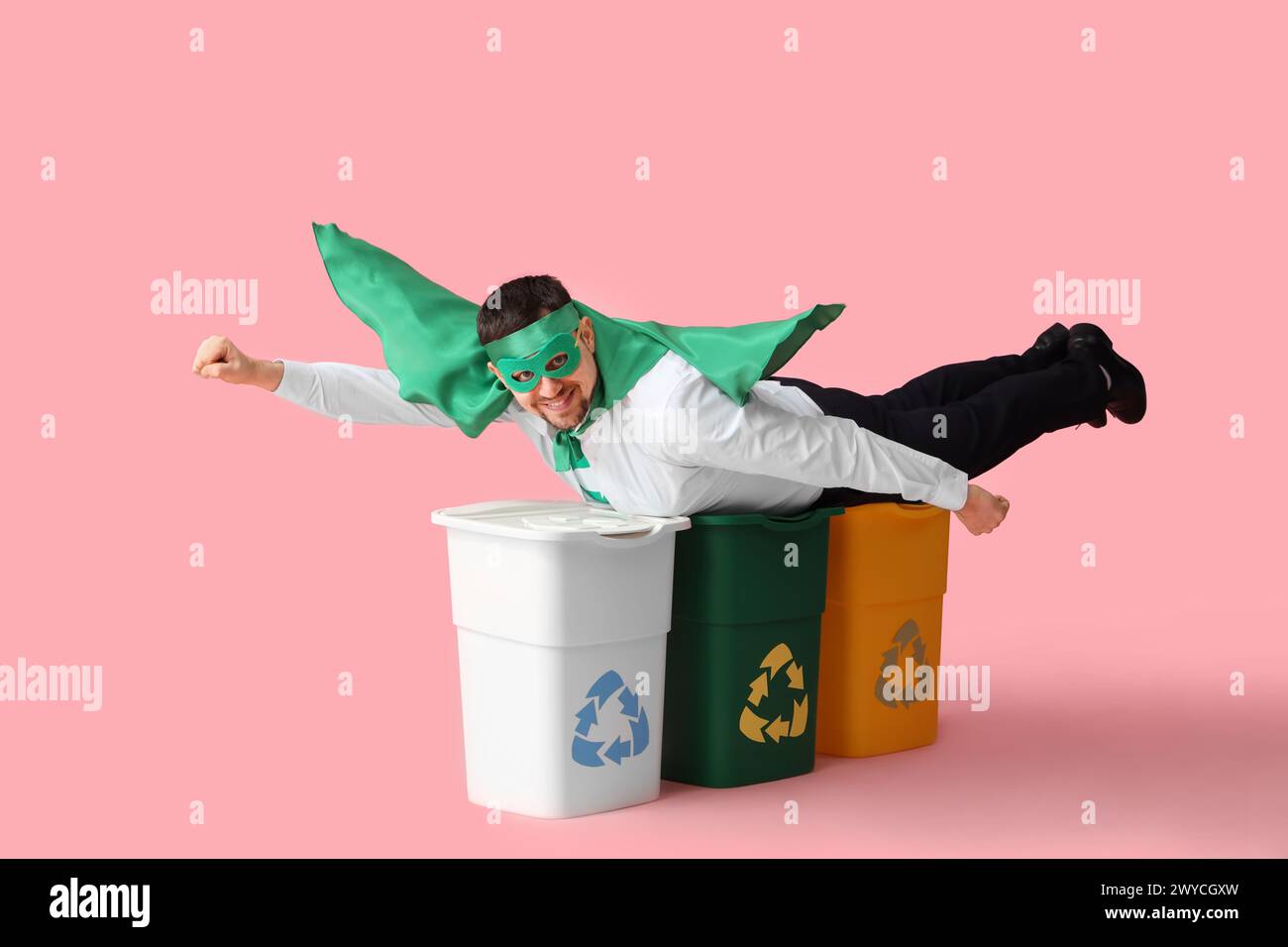 Young man dressed as eco superhero flying with garbage bins on pink ...