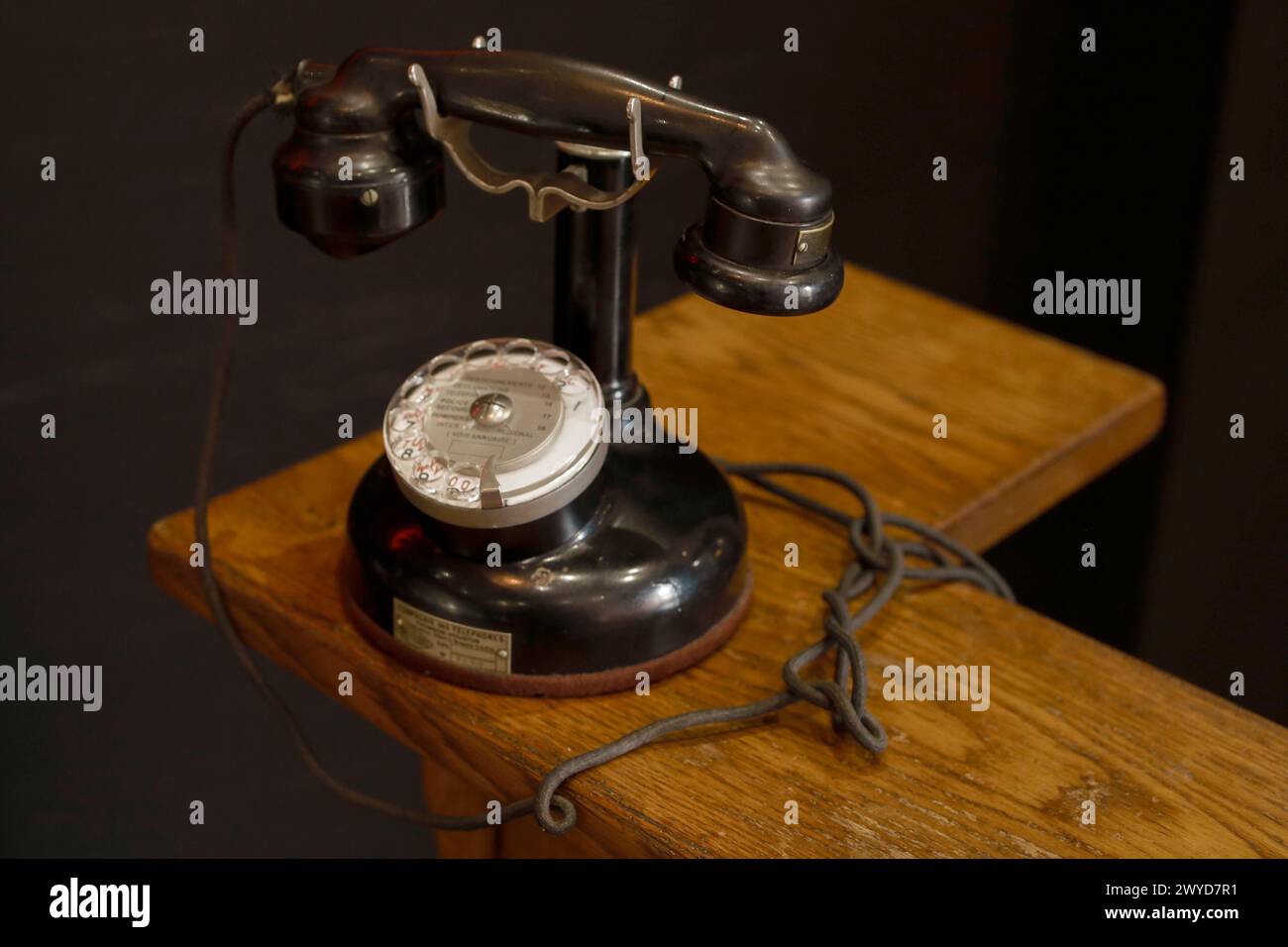 A classic, black rotary dial telephone rests on a wooden shelf, evoking ...