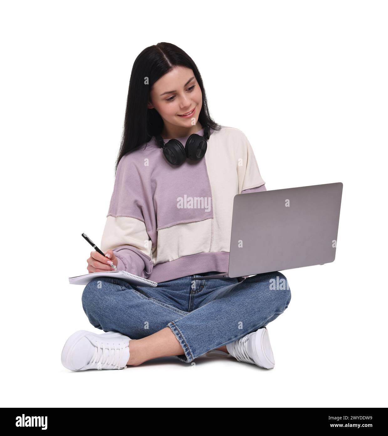 Smiling student with laptop writing in notebook on white background ...
