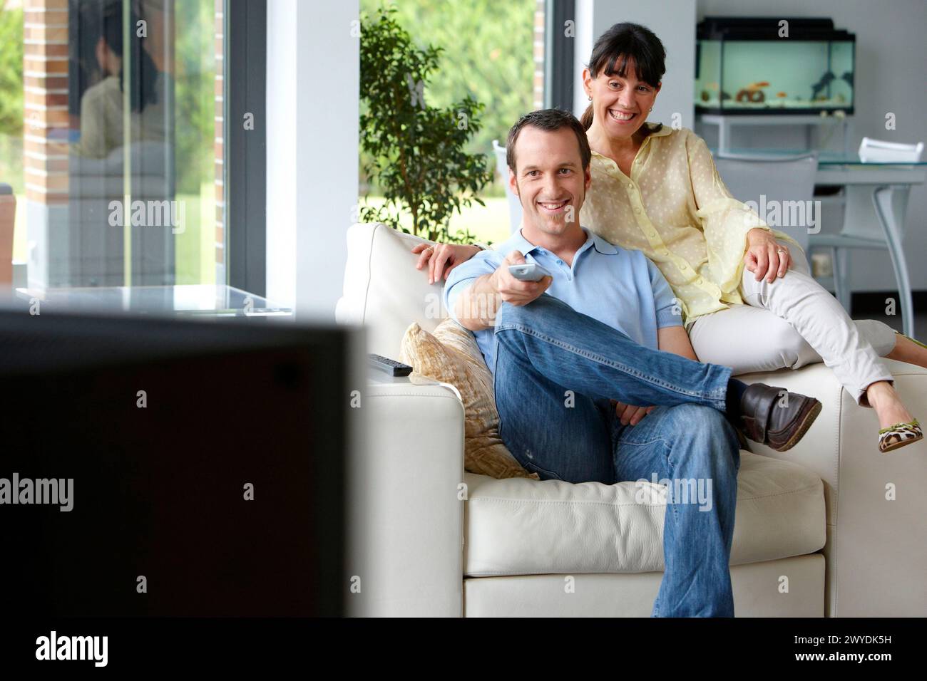 Couple sitting on coach watching TV in the living room Stock Photo - Alamy