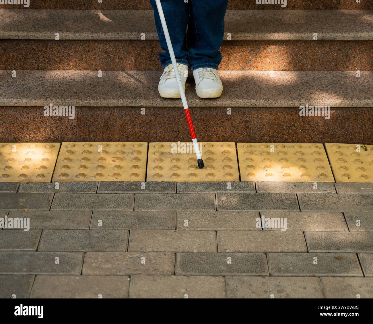 Close-up of female foot, walking stick and tactile tiles. Blind woman ...
