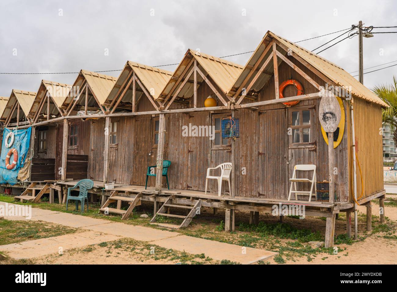 Weathered wooden beach huts adorned with nautical decor stand on stilts ...