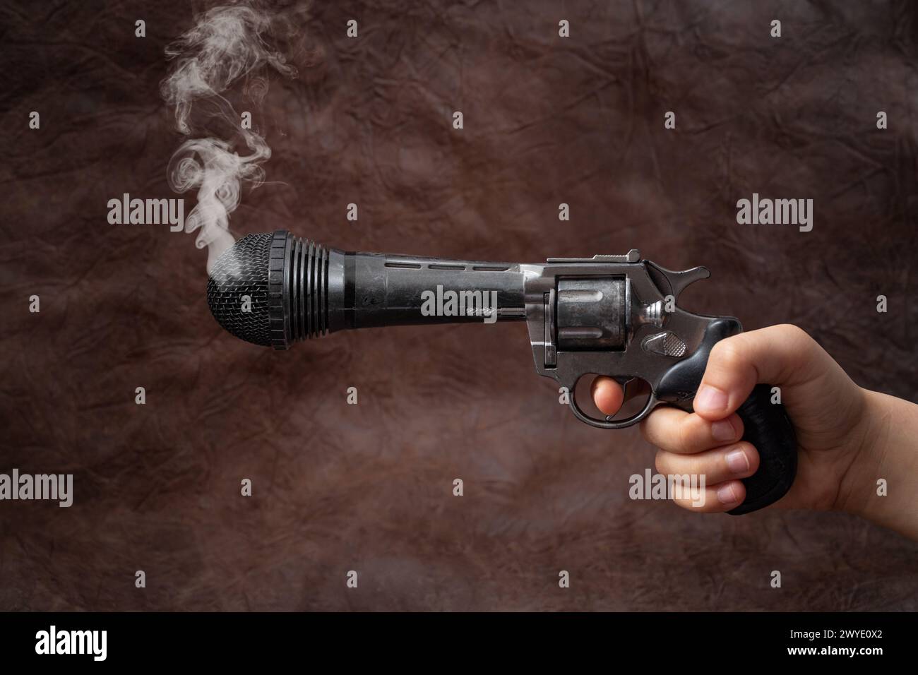 Revolver with a microphone barrel in a child hand and smoke, on brown ...