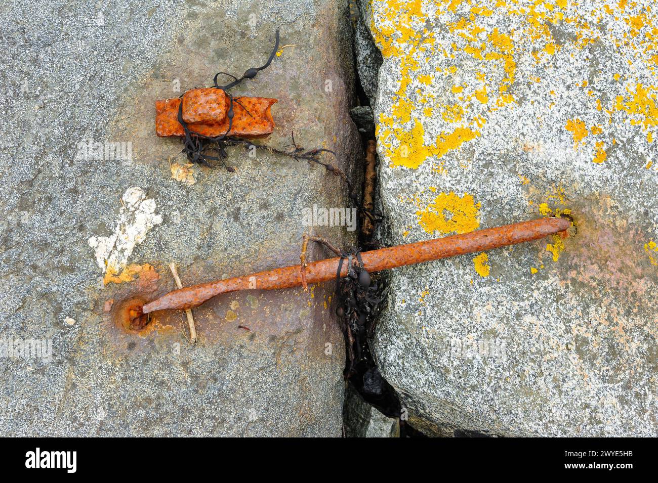 An old, rusted anchor embedded in a cracked stone with lichen growth on ...