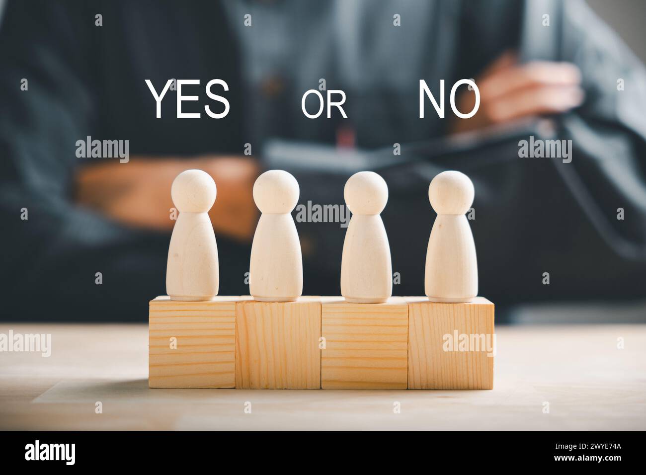 Peg dolls on wooden cube depict yes or no choices. Man's hand holds two ...