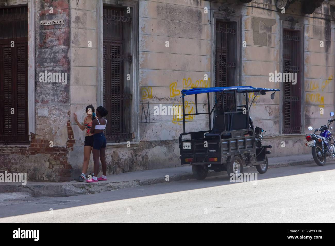 Two Cuban women talking by a trycicle and a weathered building facade in Havana, Cuba Stock ...