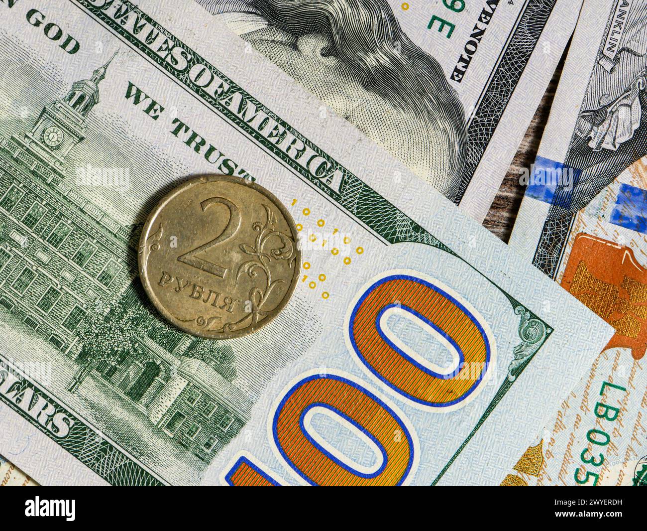 A two-ruble metal Russian coin lies on 100 dollar bills, top view ...