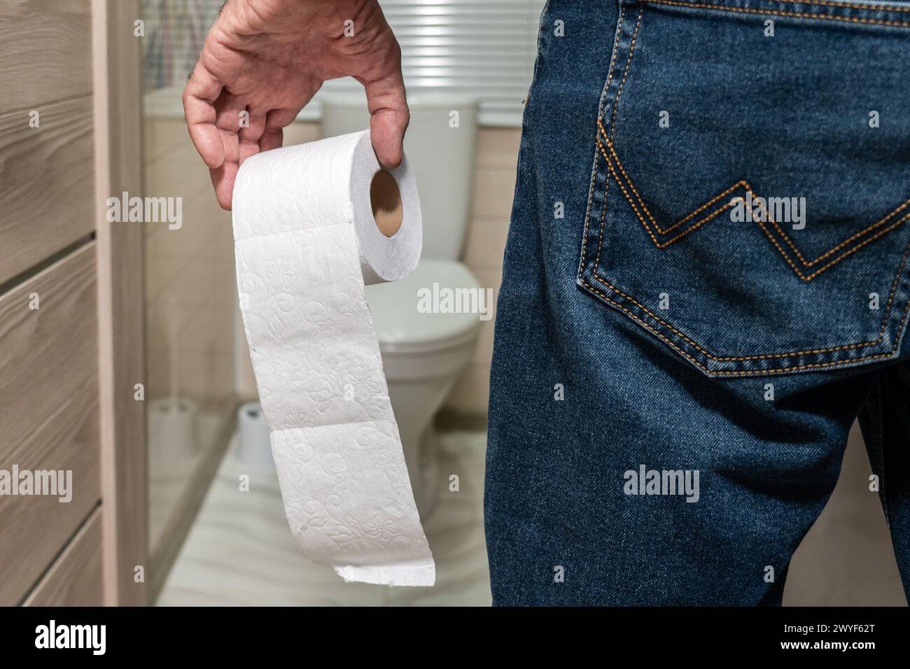 An older man's hand holding a roll of toilet paper in front of the ...