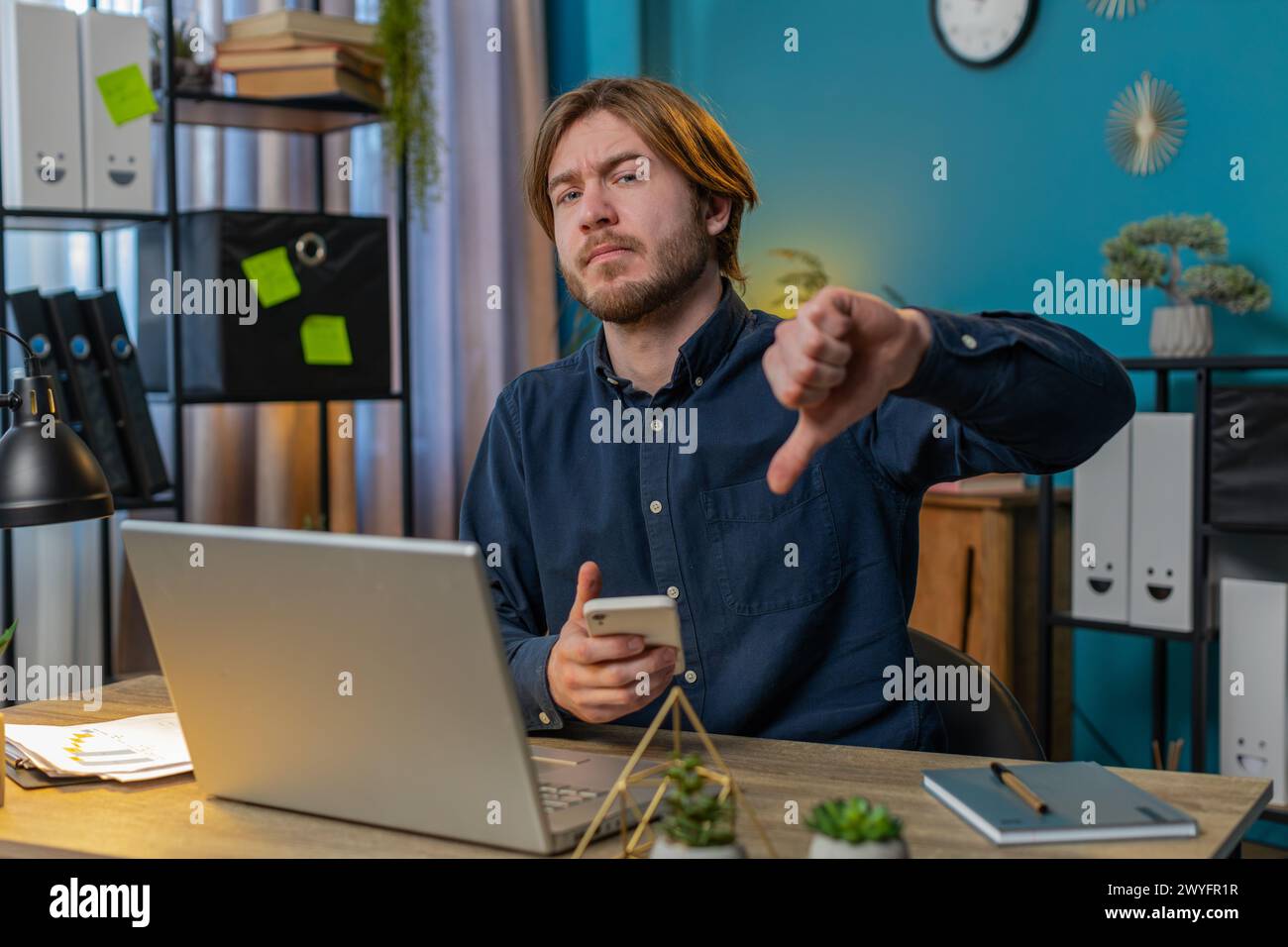 Dislike. Upset bored Caucasian businessman using smartphone at home ...