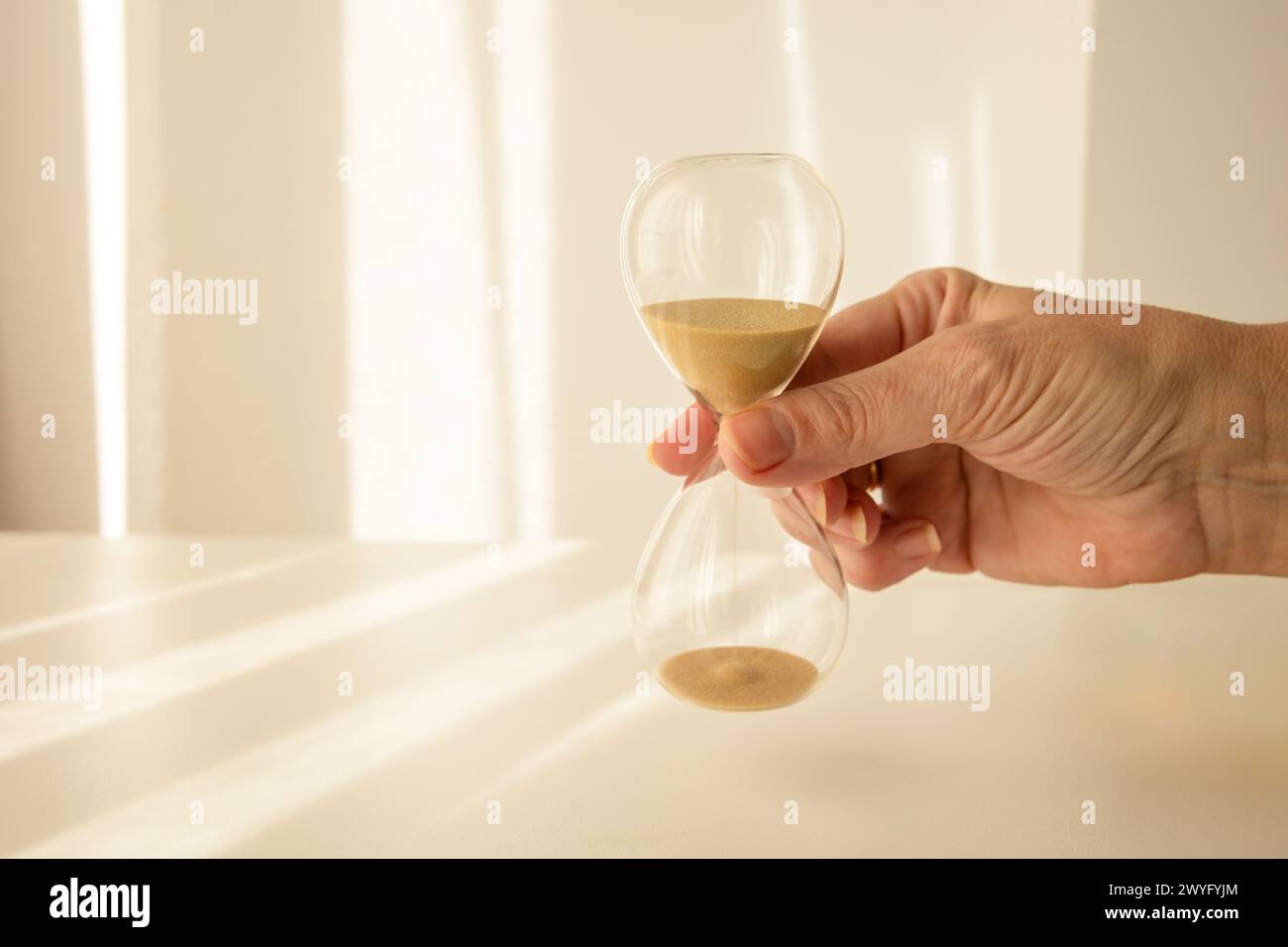 woman's hand holding time, depicted on an elegant glass hourglass with ...