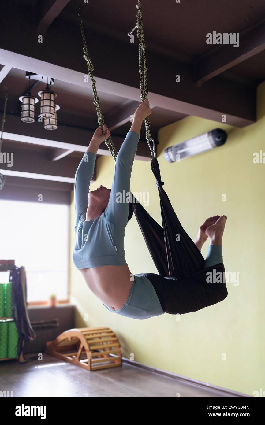 Athletic woman practicing yoga in a hammock, performing Dhanurasana ...