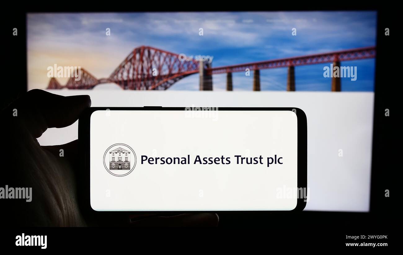 Person holding cellphone with logo of British investment company Personal Assets Trust plc in ...