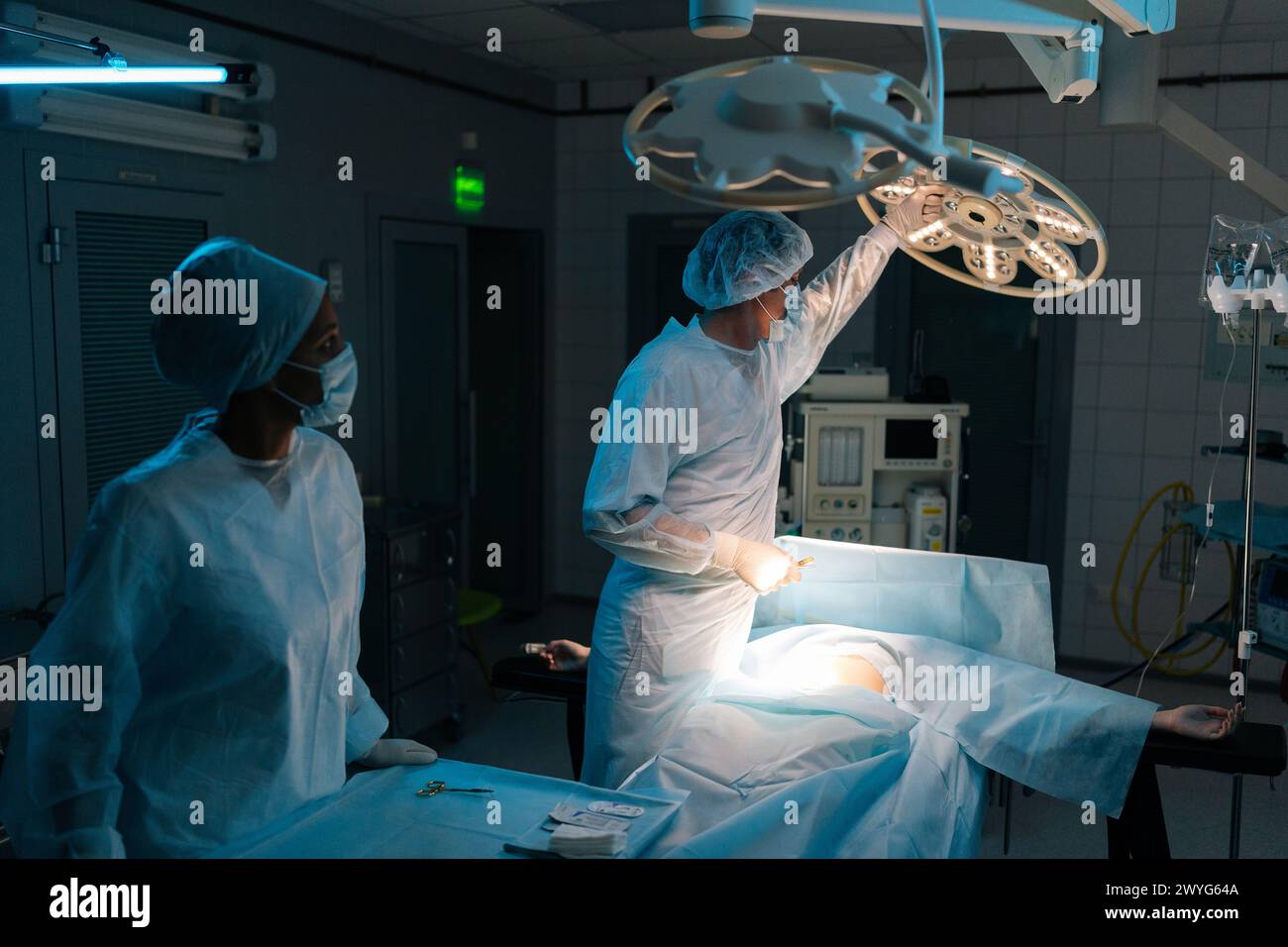 Male plastic surgeon in surgical uniforms and masks adjusting light ...