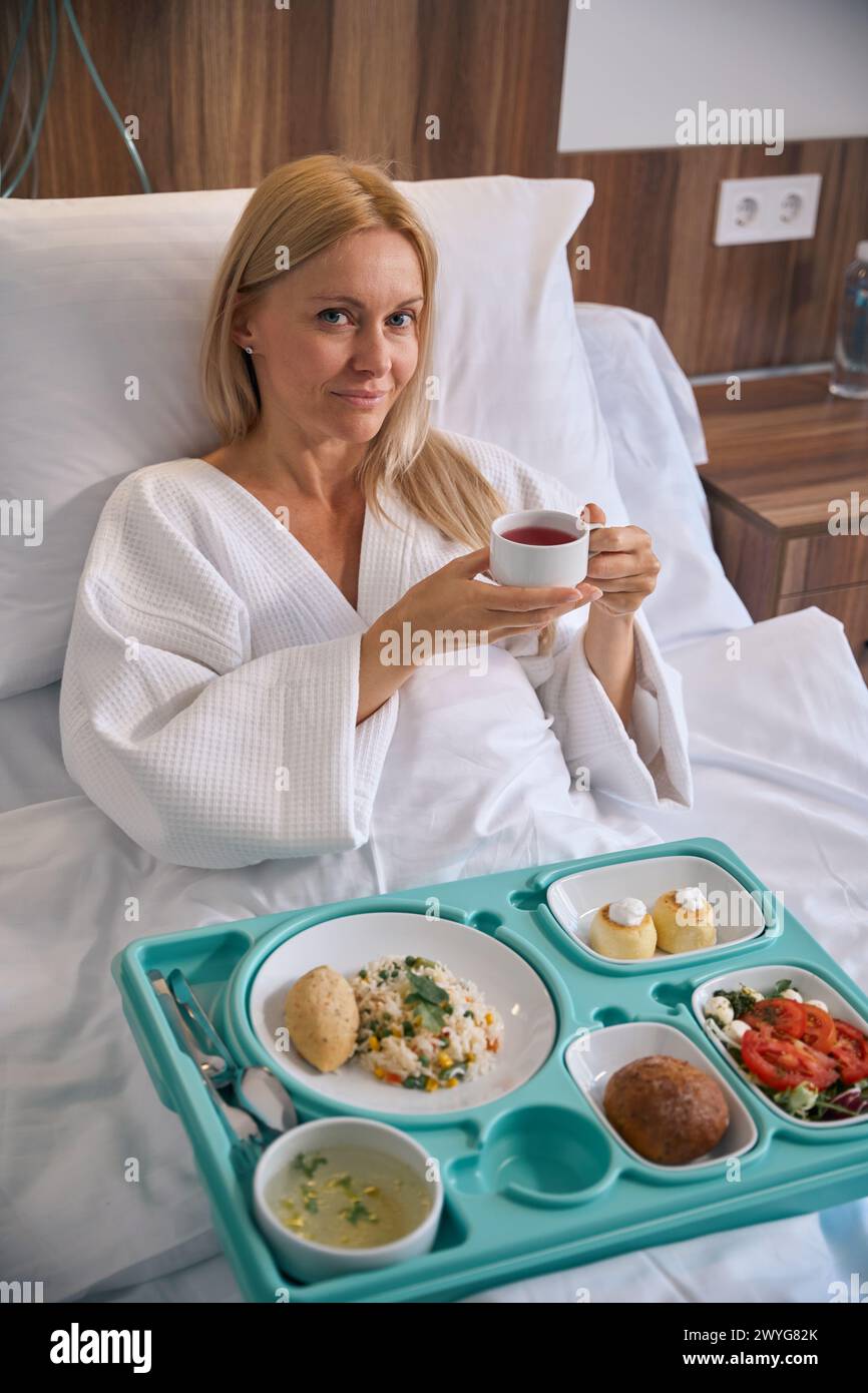 Pleased inpatient having tea during lunchtime in private clinic ward ...