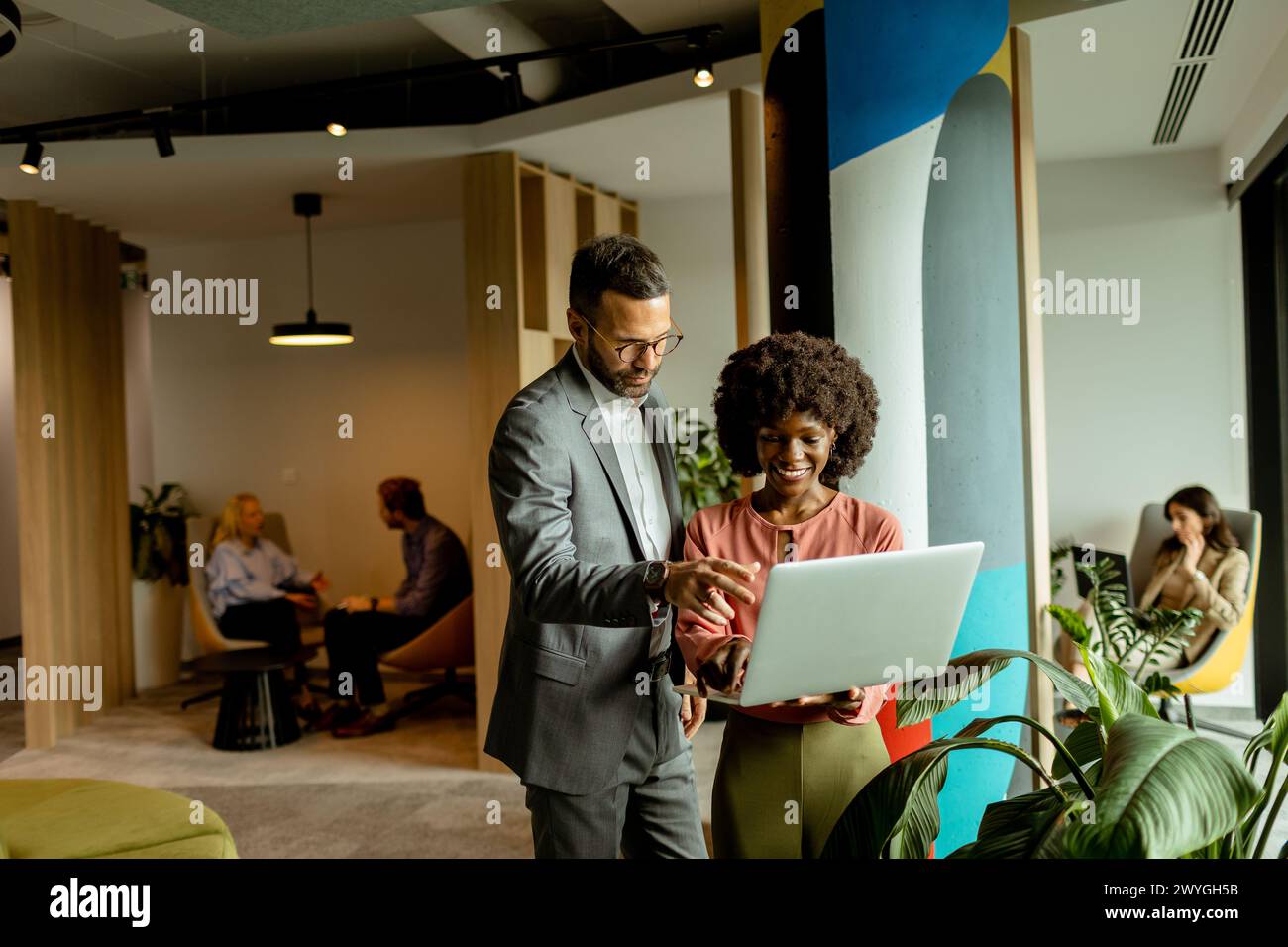 Man and woman discuss work on a laptop in a vibrant office setting ...