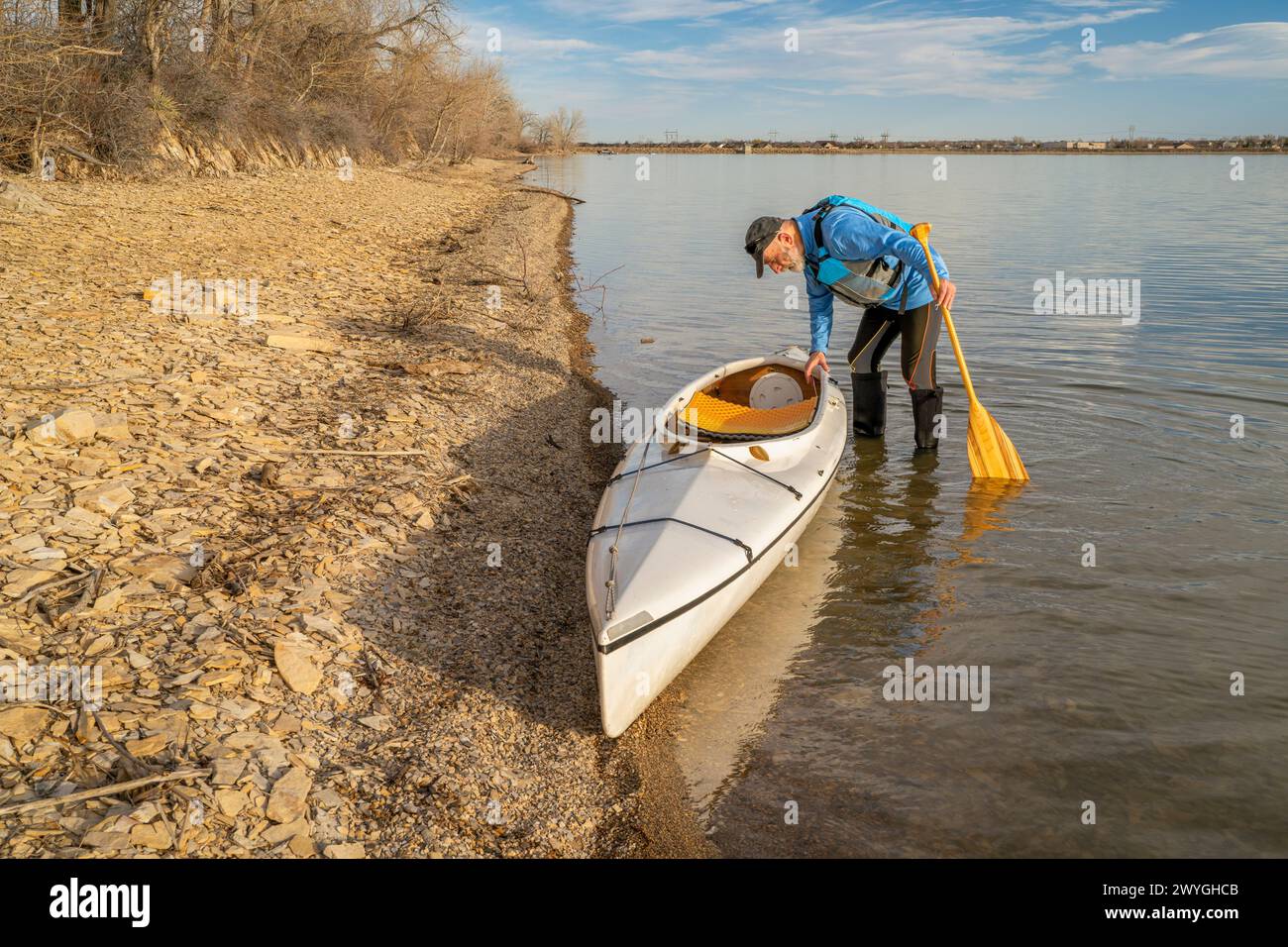 senior male paddler with expedition decked canoe on a lake shore in ...