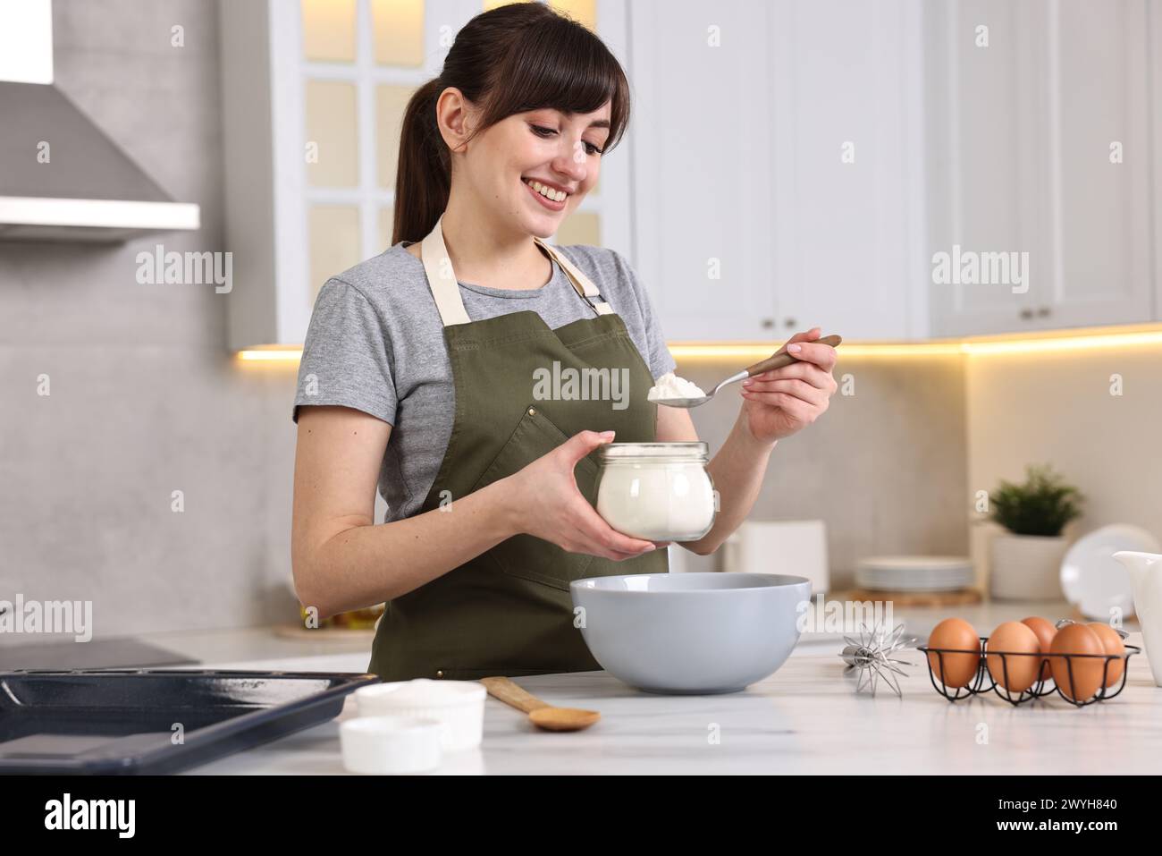 Happy young housewife adding flour into bowl at white marble table in ...