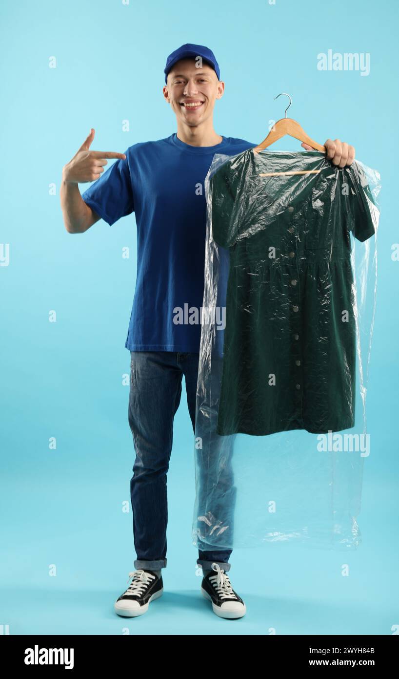 Dry-cleaning delivery. Happy courier holding dress in plastic bag on ...