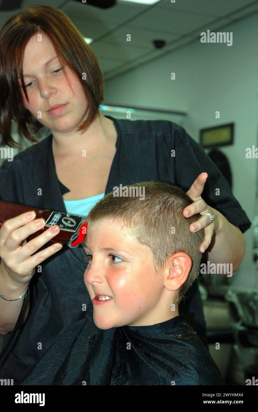 A female hair dresser gives a young boy a buzz cut at a faircut salon ...
