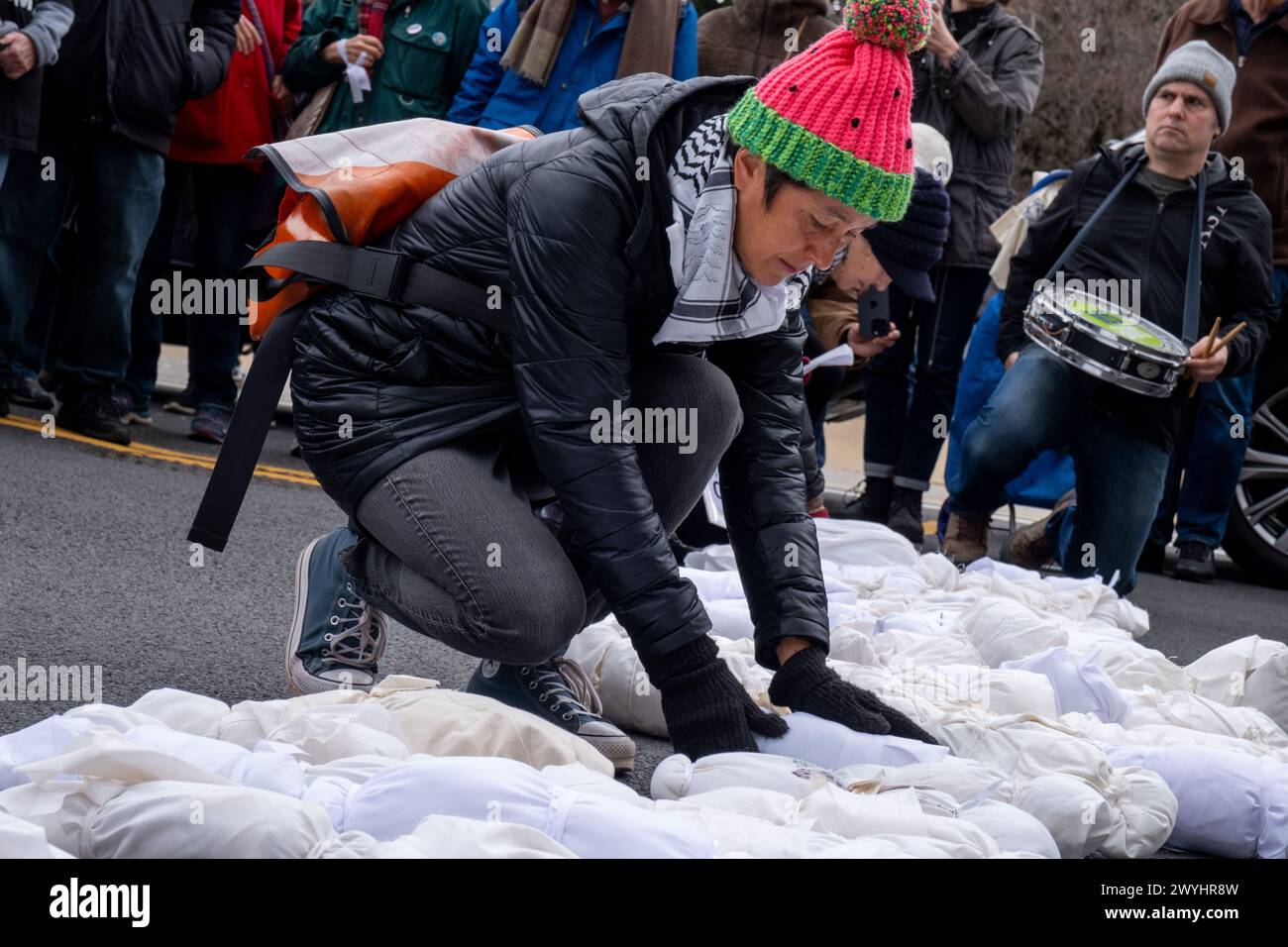 A woman wearing a watermelon hat and keffiyeh lays down an effigy of a ...