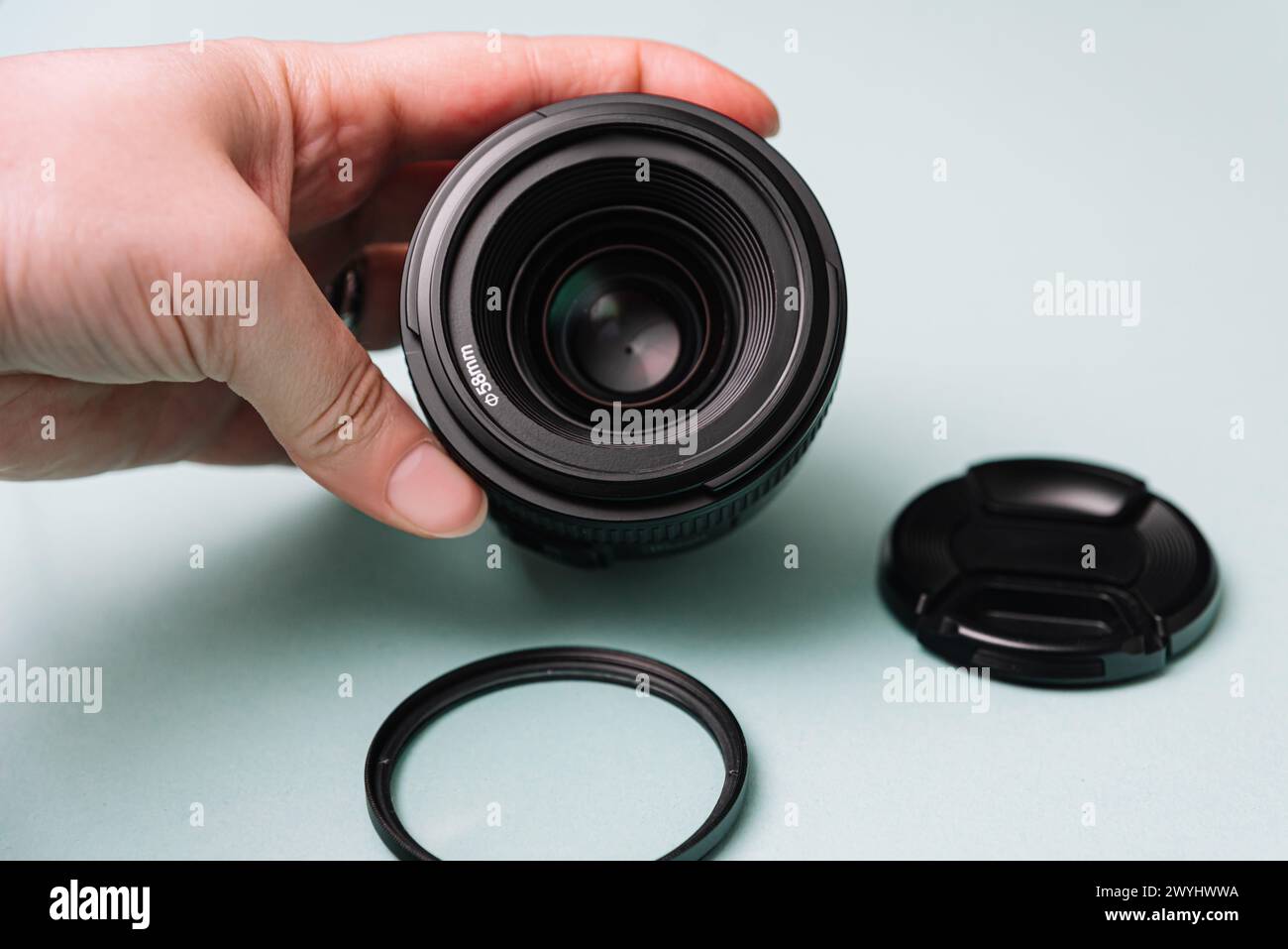 Close-up of a hand holding a DSLR lens with its cap and a UV filter ...