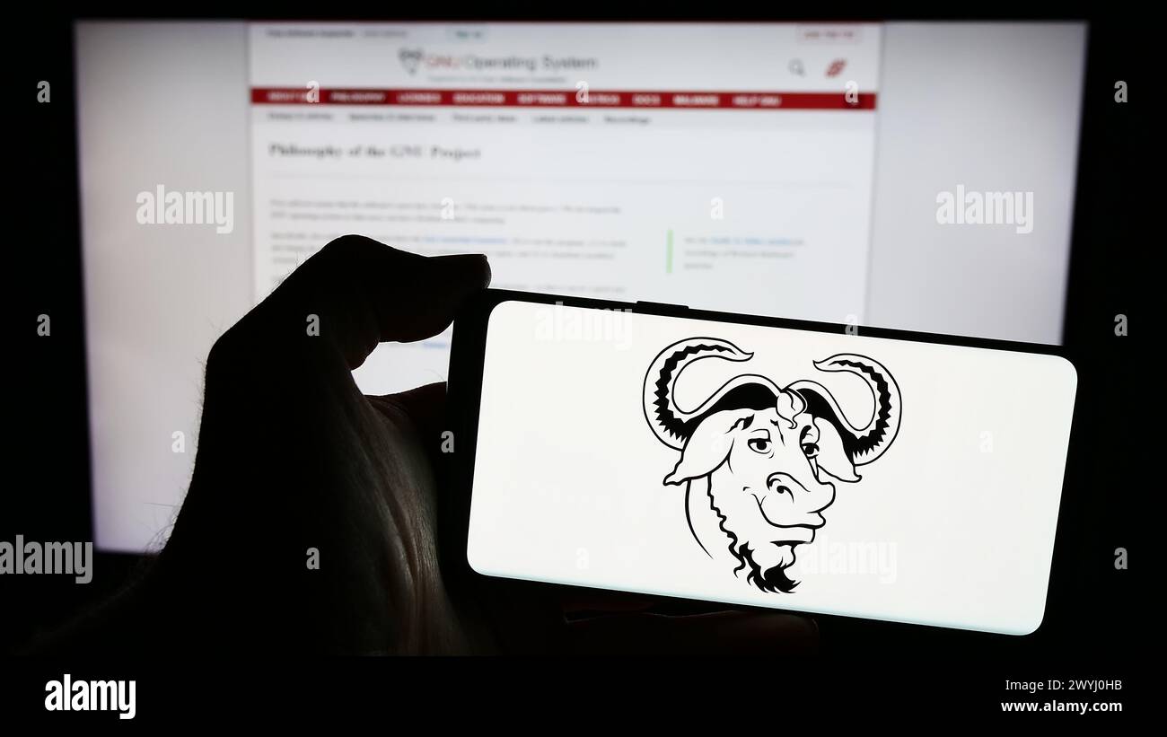 Person holding mobile phone with logo of software collaboration project GNU Project in front of ...