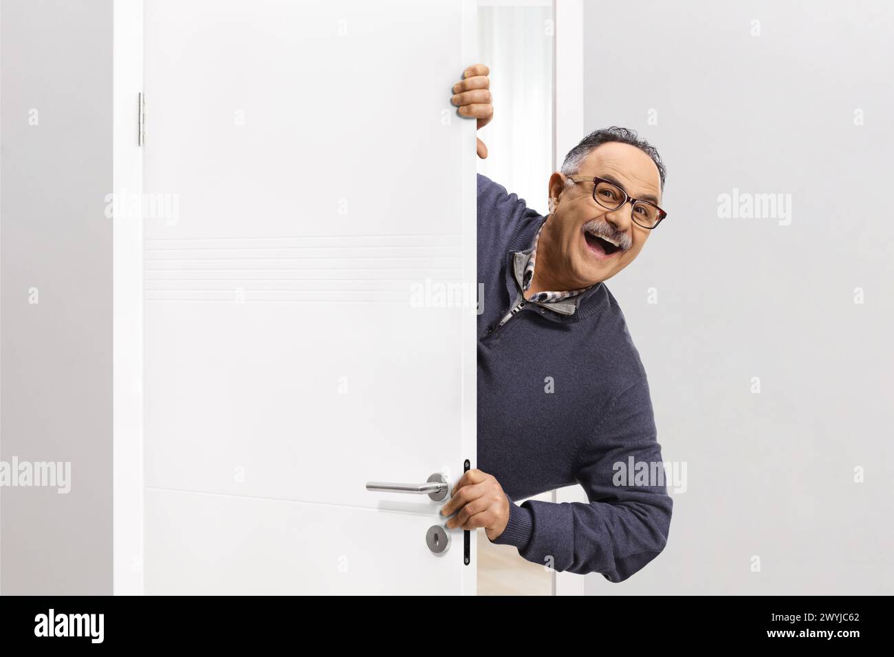 Cheerful mature man hiding behind a door isolated on white background ...