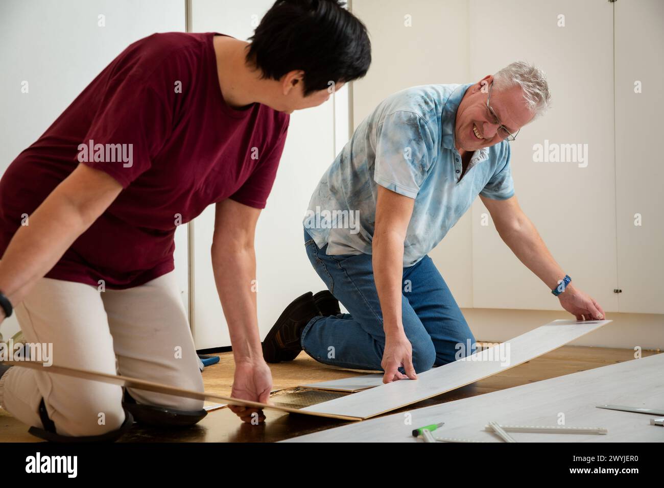 Senior couple installing laminate flooring in their new home together. DIY concept. Mature woman ...