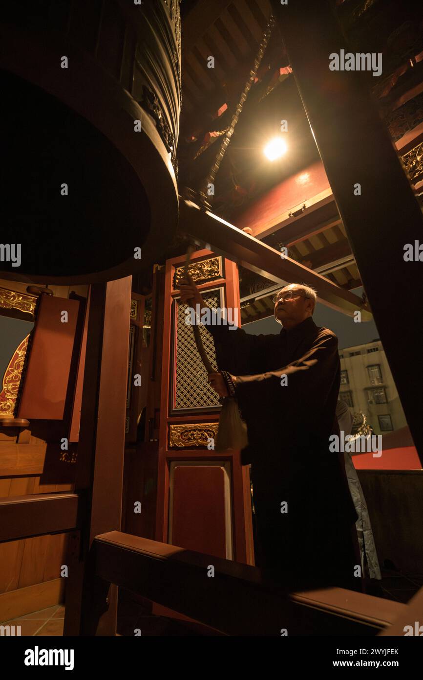 A monk in traditional attire ringing a large bell in Baoan temple ...