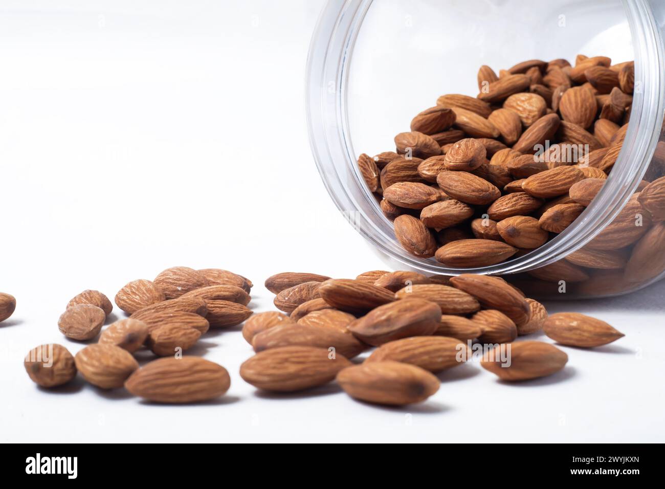 Almonds falling from a glass container leaning against a white ...