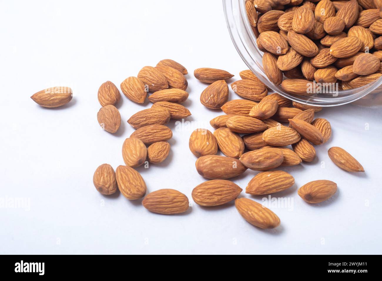 Almonds falling from a glass container leaning against a white ...
