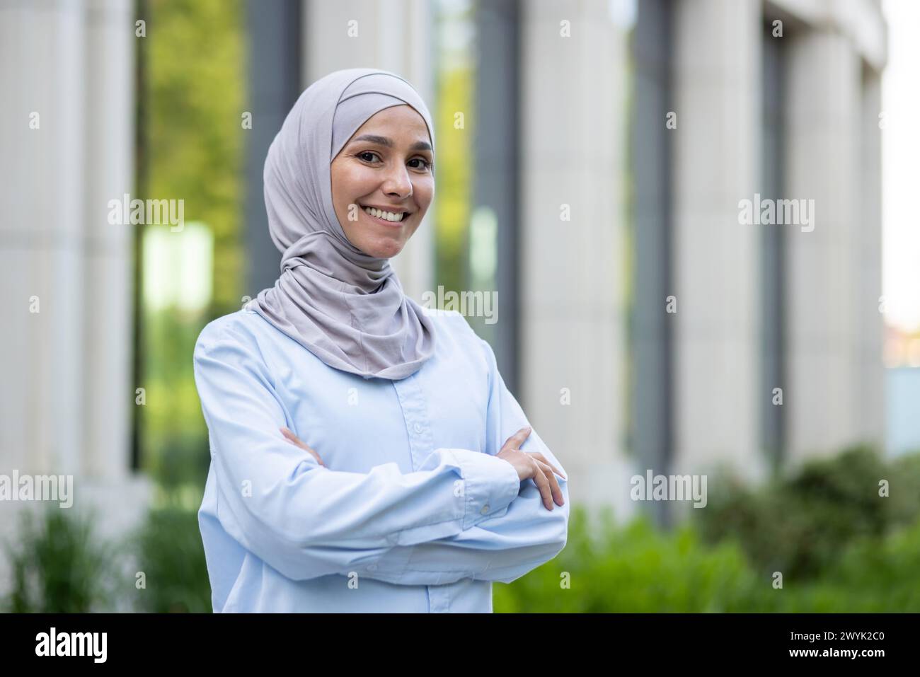 A professional Muslim woman in a hijab stands confidently outdoors with ...