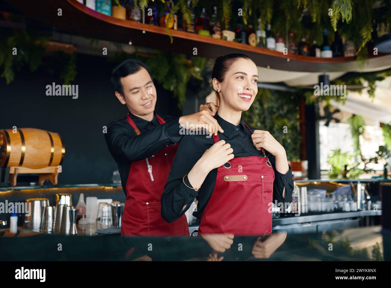 Friendly bartender helping coworker to adjust apron strap Stock Photo ...