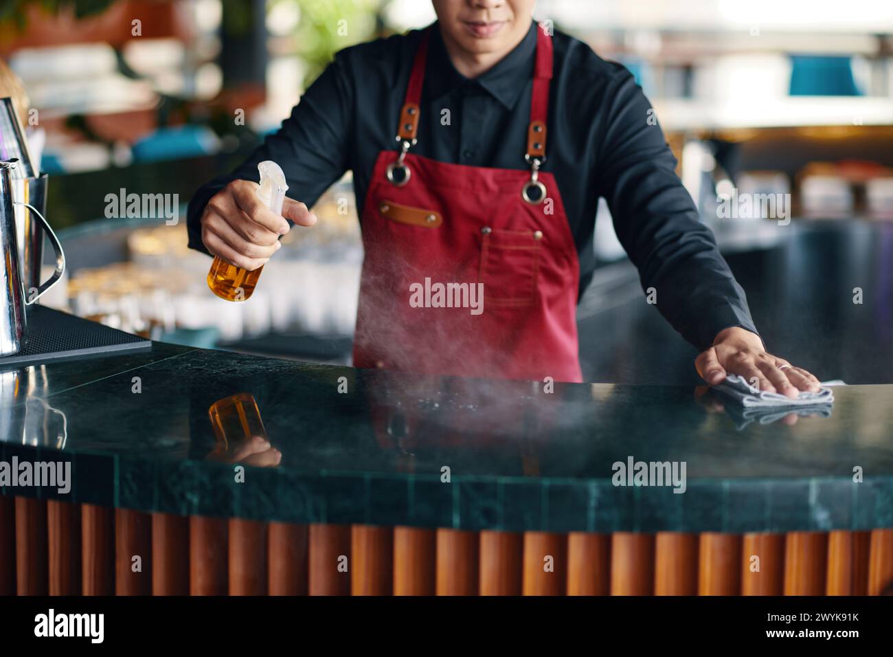 Cropped image of waiter cleaning bar counter with disinfecting spray ...