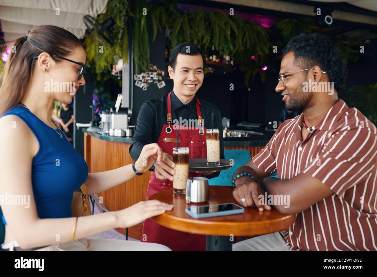 Coffeeshop barista bringing iced coffee to smiling couple Stock Photo ...