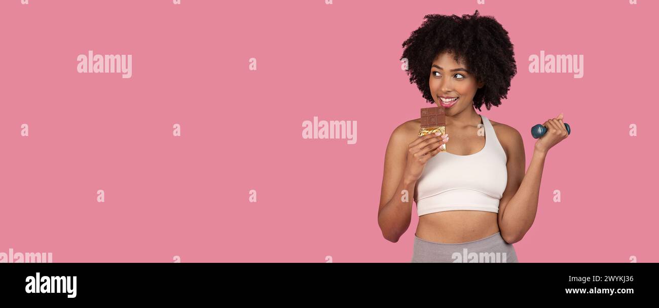 Woman eating chocolate and holding dumbbell Stock Photo - Alamy