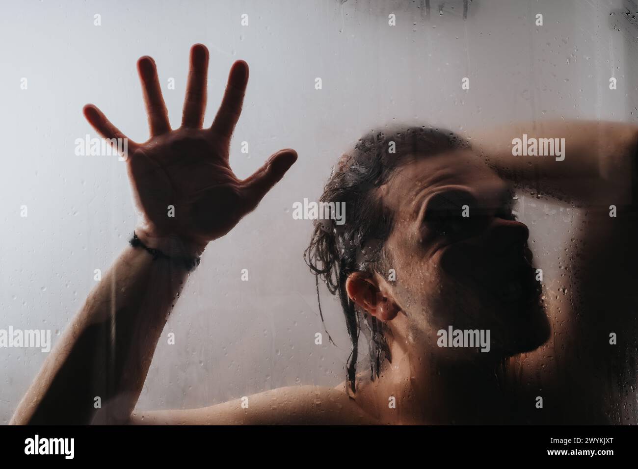 Man pressing hand against steamed glass shower door with thoughtful ...