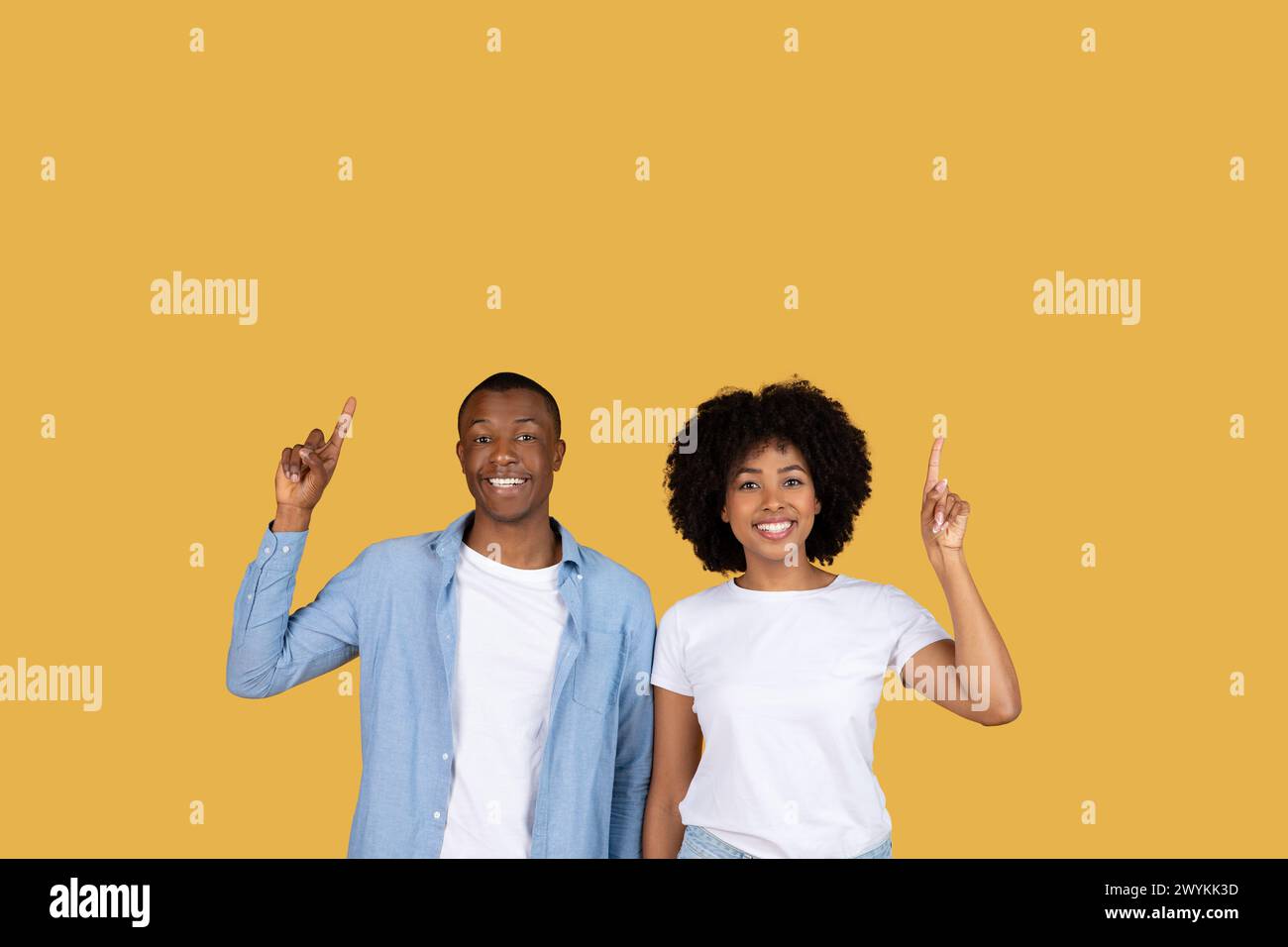 Two people pointing upwards, smiling on yellow Stock Photo - Alamy