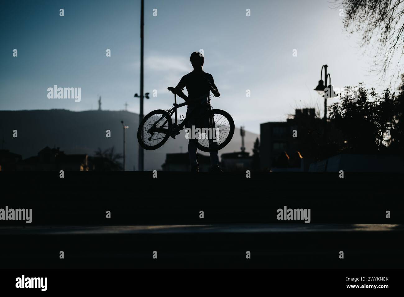 Silhouetted man with bicycle in park at dusk, serene outdoor scene ...