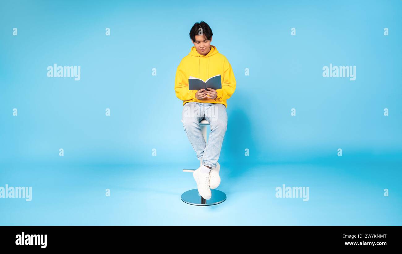 Concentrated teen reading a book on a stool Stock Photo - Alamy