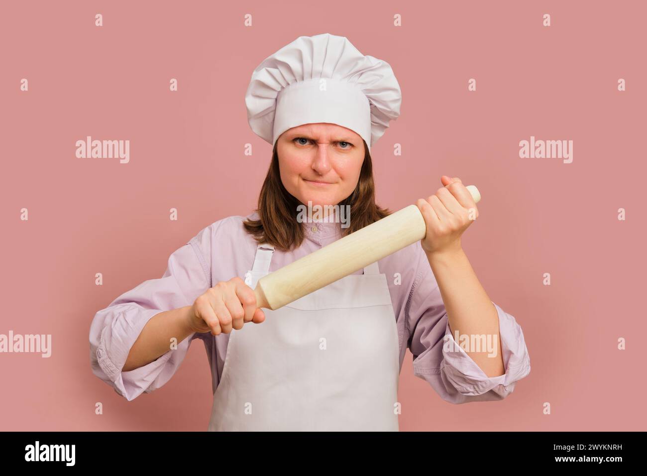 Angry woman cook on studio pink background. Portrait of a female person ...
