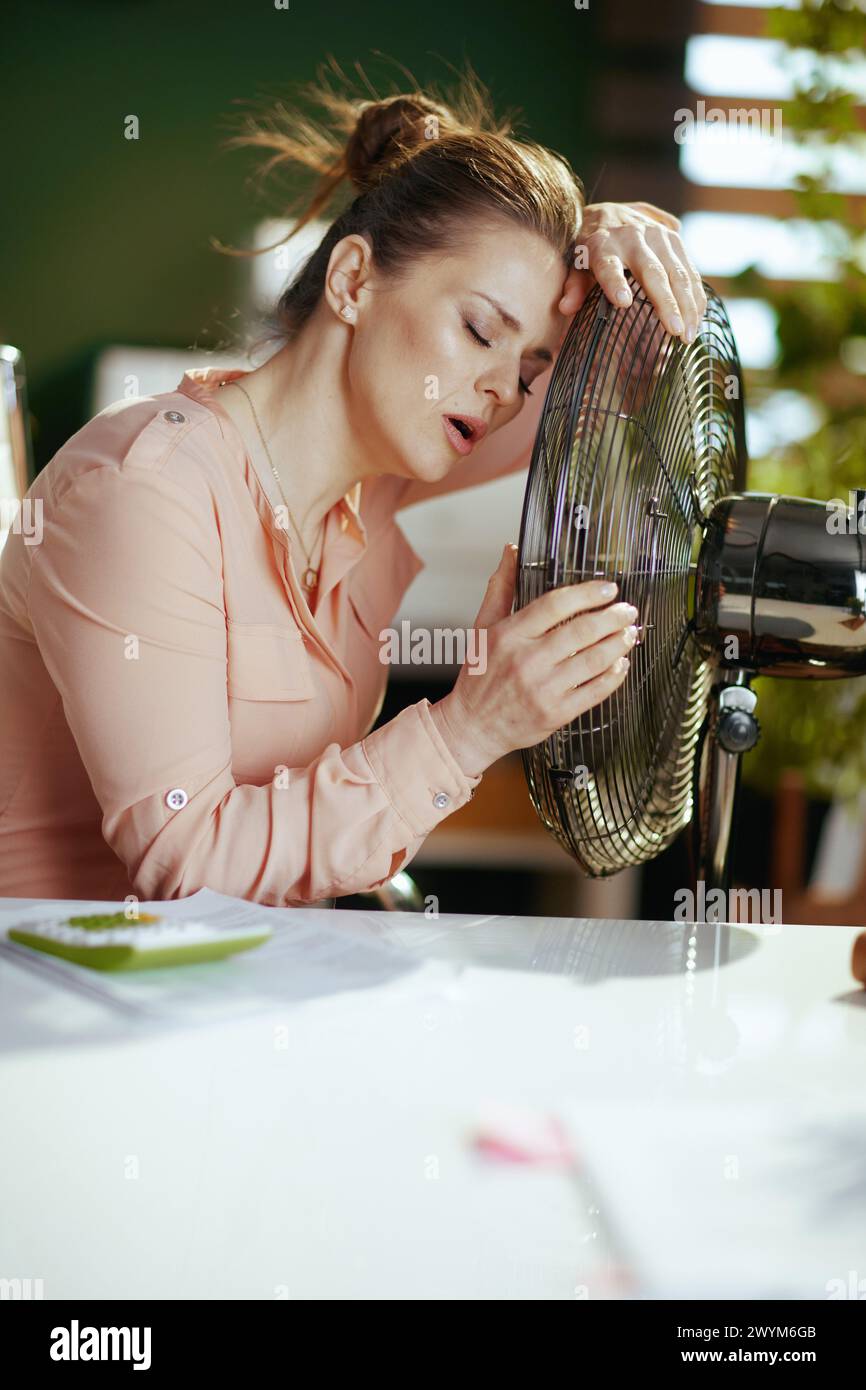 Sustainable workplace. modern middle aged business woman at work with electric fan suffering ...
