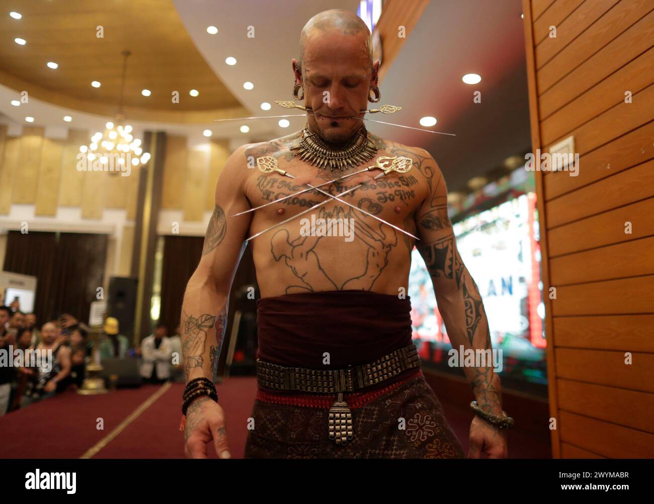 A man with multiple needle piercings on his face and chest walks down ...