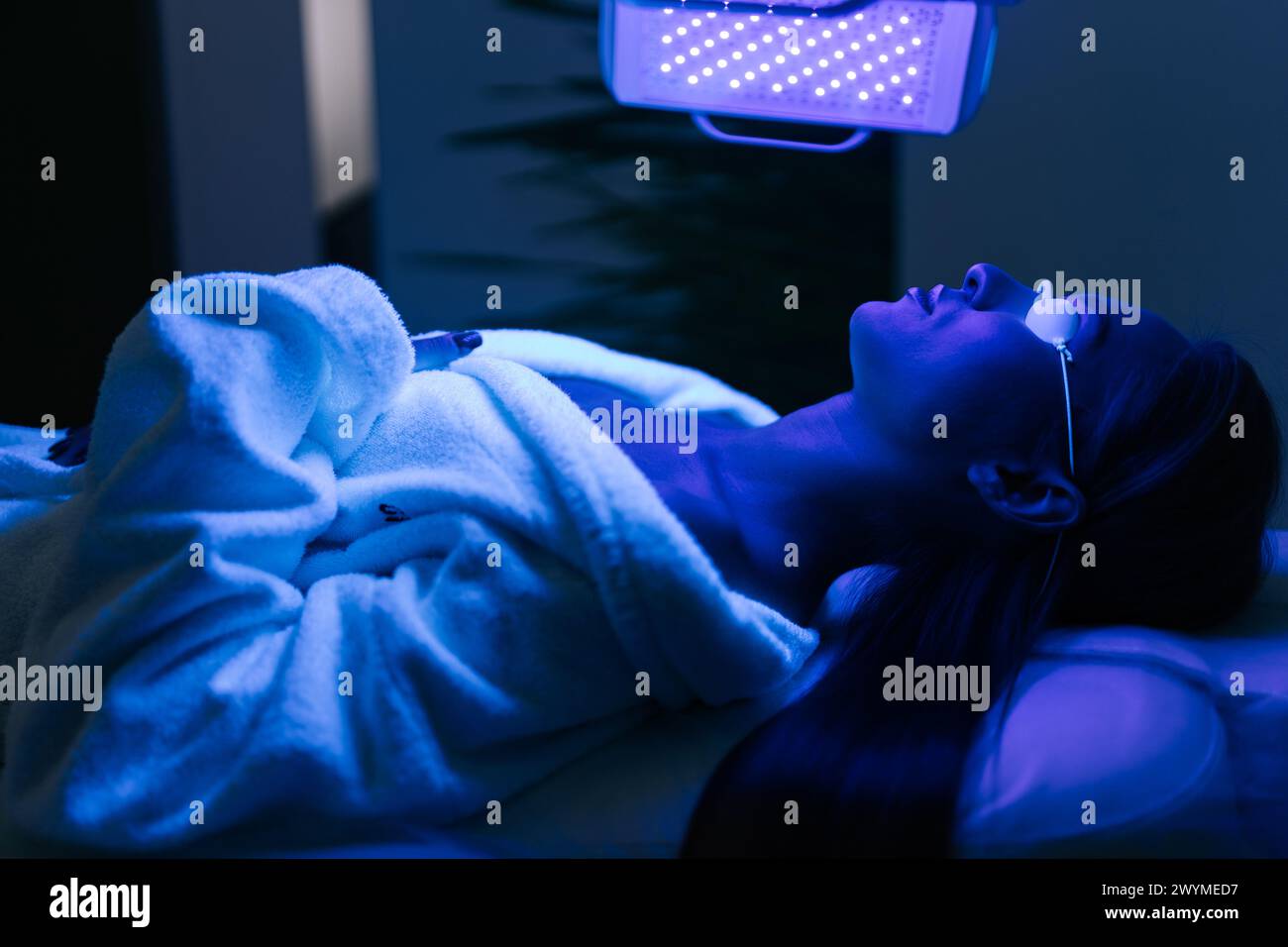 Young woman in glasses having blue LED light facial photodynamic ...