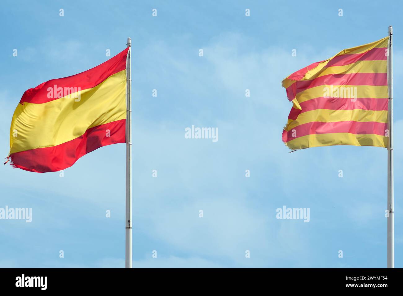 The image shows the flags of Catalonia and Spain waving together in a ...