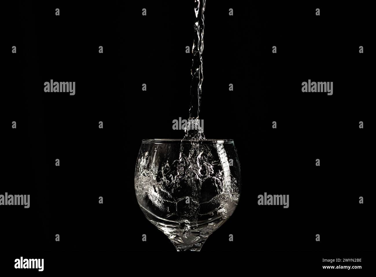 Stream of water in drops falling into a glass cup against a black ...