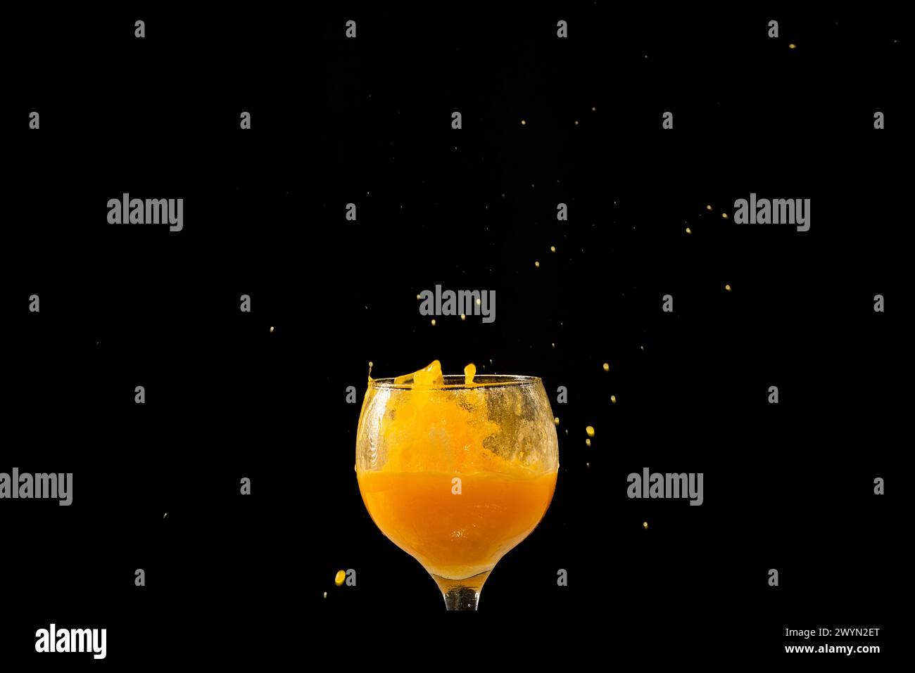 Splash in a glass goblet with orange juice inside. Isolated on black ...