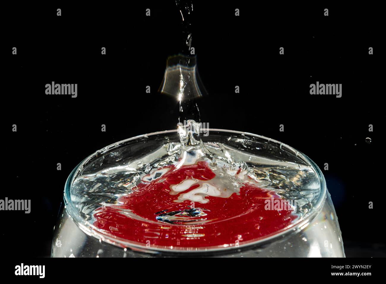 Transparent glass bowl, filled with water, with red reflection and ...